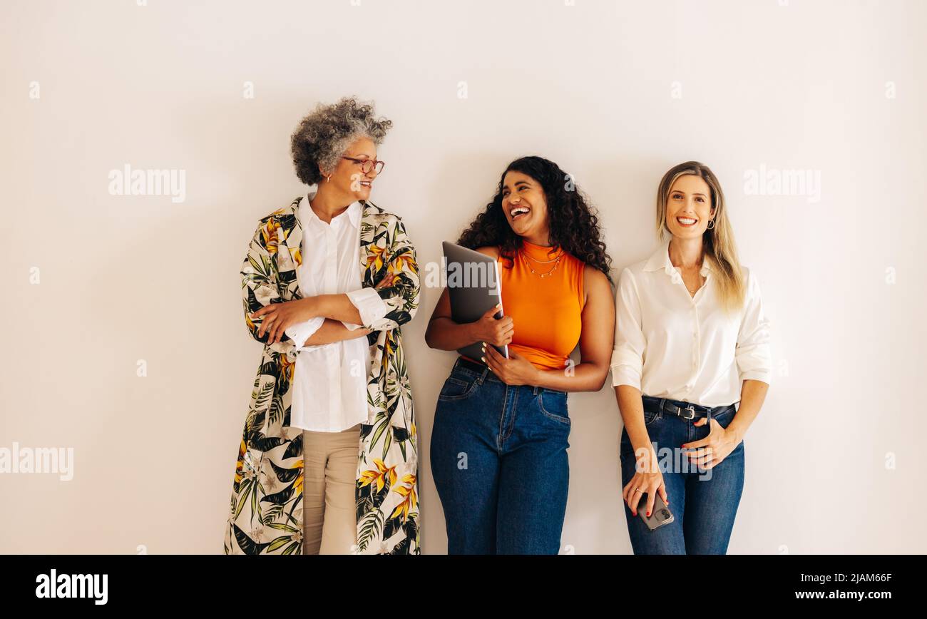 Team of happy businesswomen smiling cheerfully while standing against a ... Team of happy businesswomen smiling cheerfully while standing against a ...