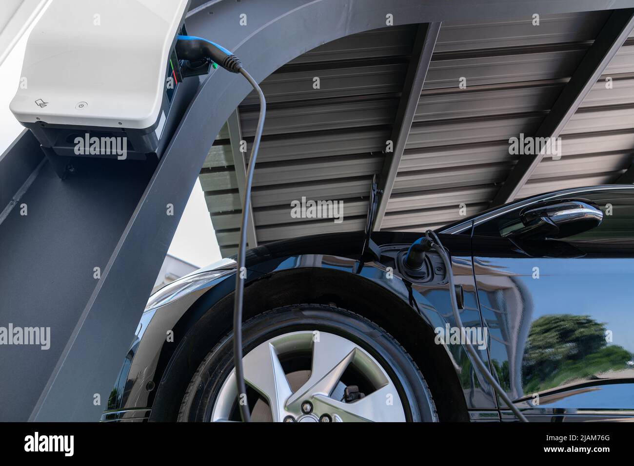 Electric car is charged from a charging station at carport that takes ...