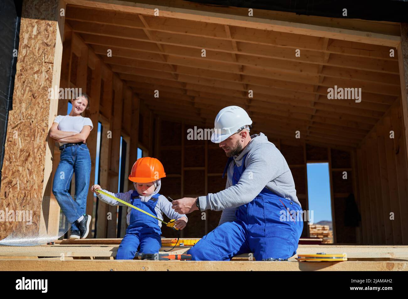 Father, mother and son building wooden frame house. Toddler boy helping ...
