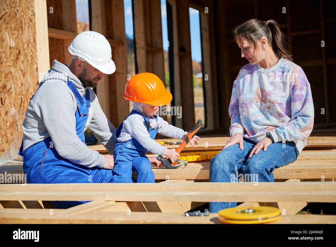 Father, mother and son building wooden frame house. Toddler boy helping ...