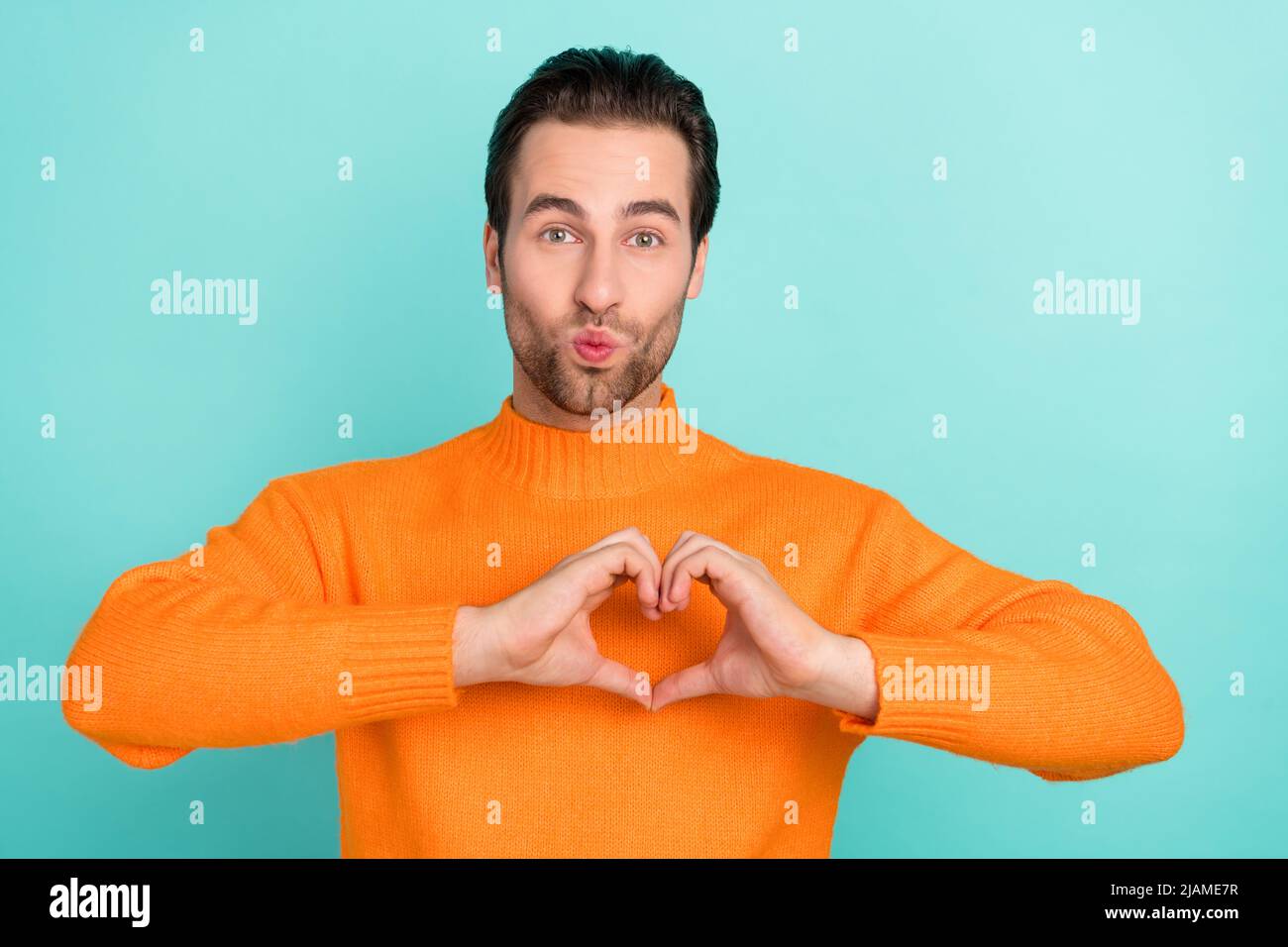 Portrait of positive young man arms make heart symbol kiss lips look ...