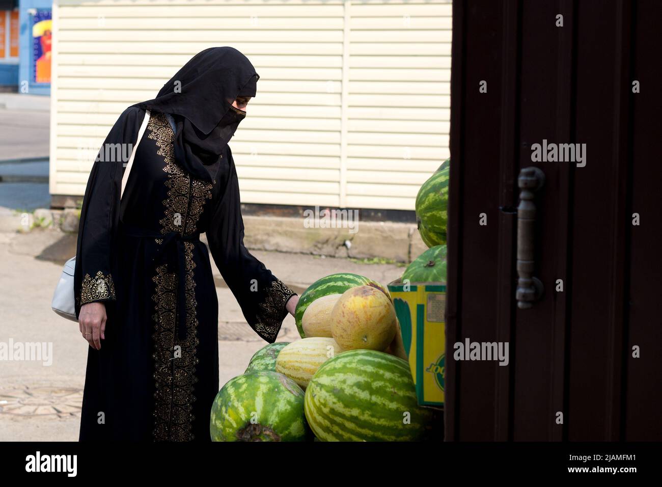 A Muslim woman in national clothes inspects watermelons and melons city ...