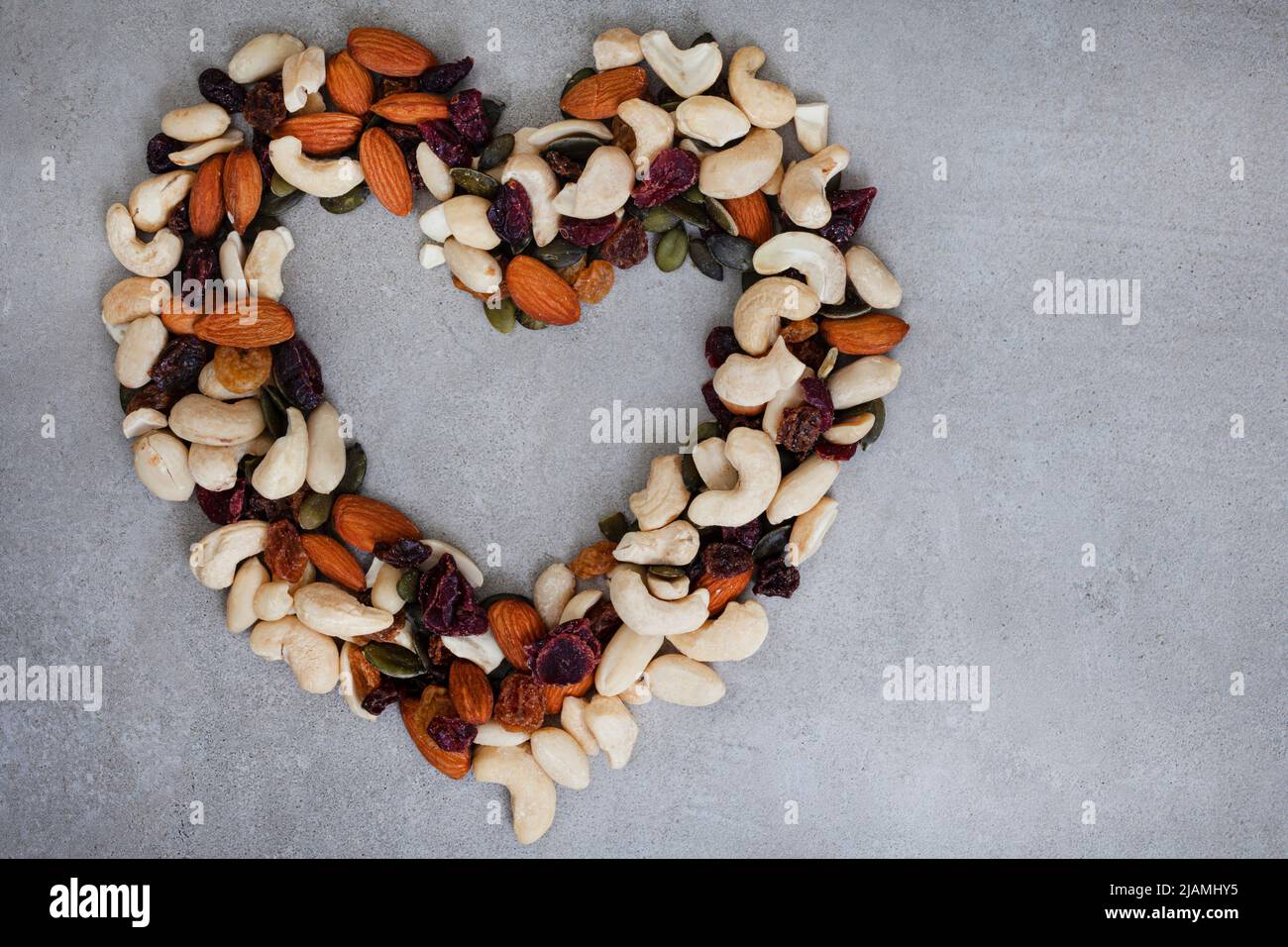 heart shape made of nut and fruit mix on mottled grey with copy space ...