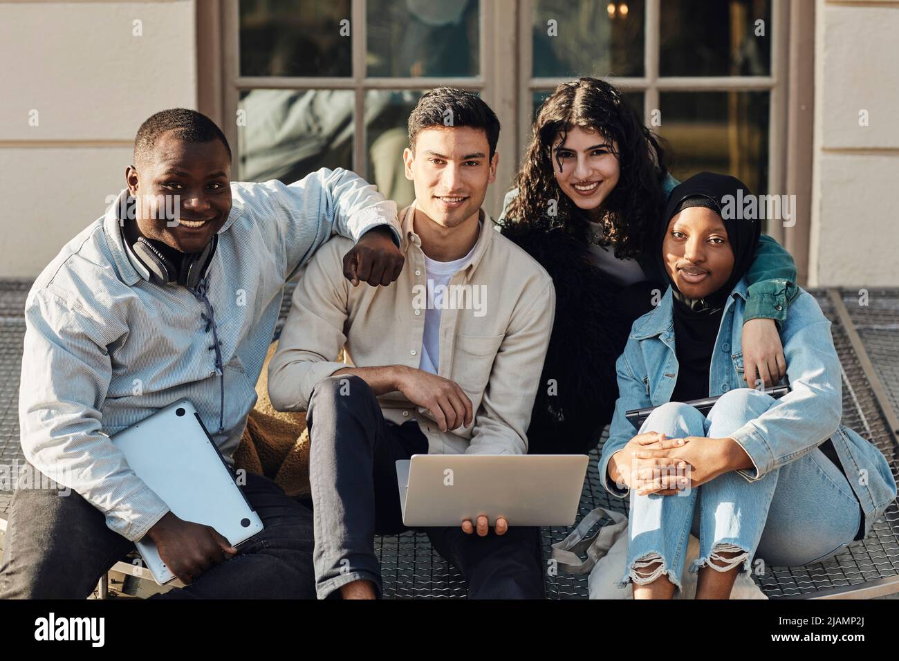 Portrait of multiracial students with laptop sitting at university ...