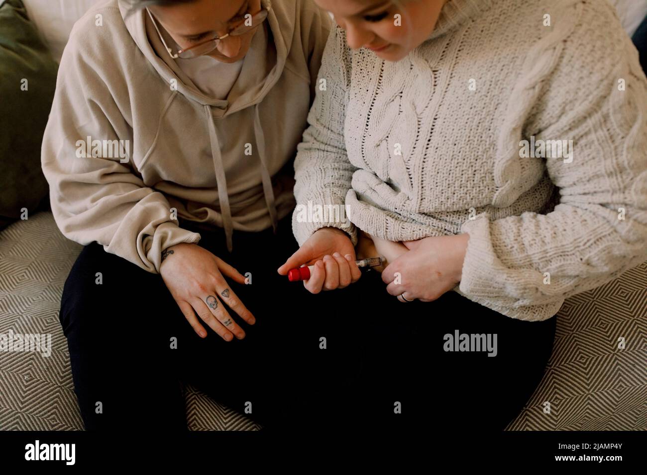 Woman with girlfriend injecting syringe in abdomen while doing IVF test ...