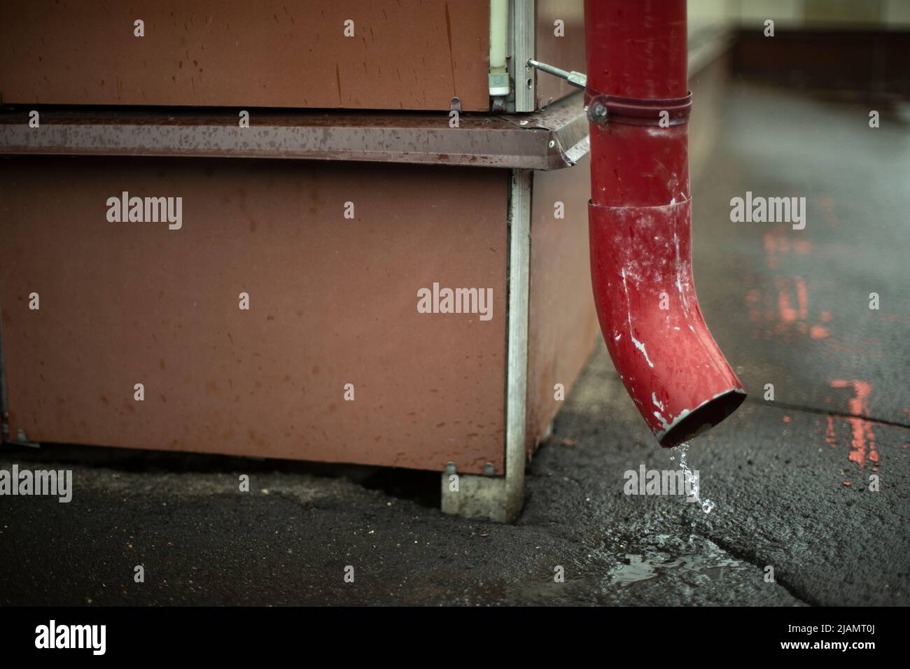 Downspout in building. Water flows from roof onto asphalt. Red pipe for ...