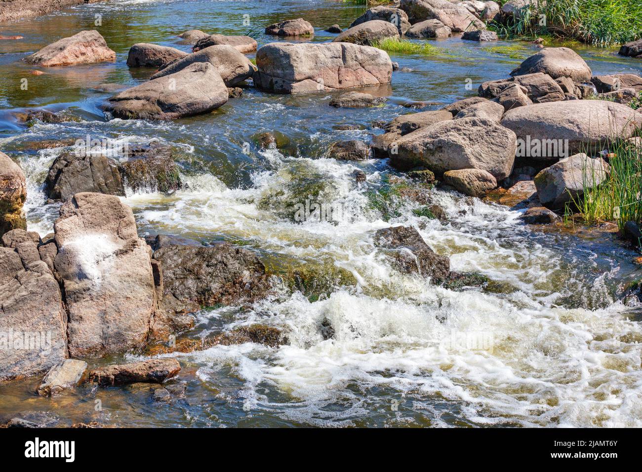Stone boulders on the path of the rapid water flow of river water on a ...