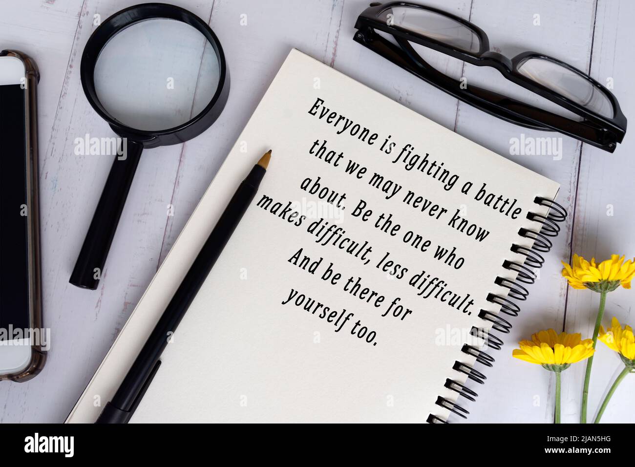 Motivational quote on black note book on wooden desk -Everyone is ...