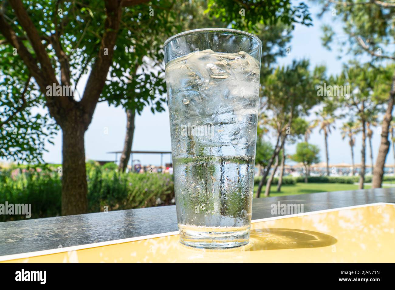 A glass of water with ice on yellow table, on nature background. Cold ...