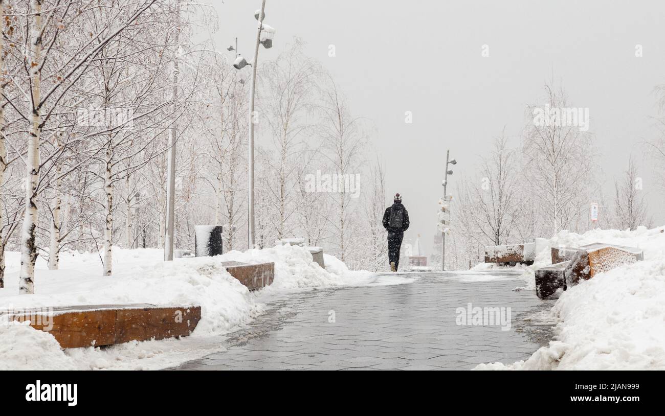 A young man t with a backpack walks on a snow-covered sidewalk during a ...