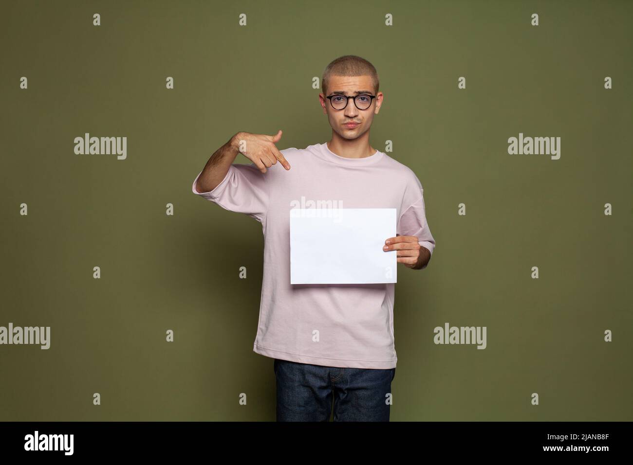 Serious young man student holding white empty paper board on green ...