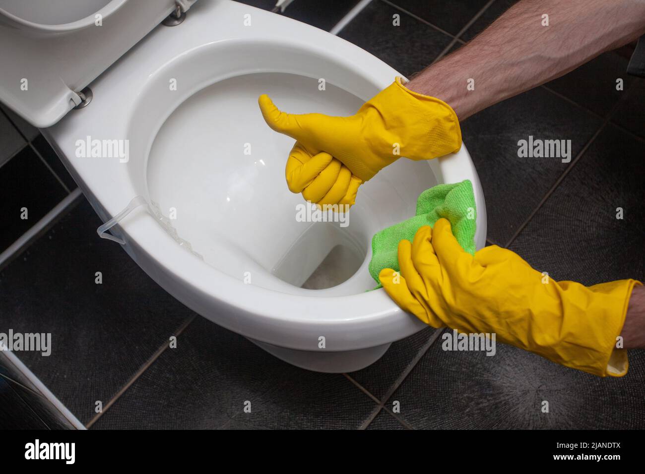 Man in rubber protective gloves cleaning and washing toilet and showing ...
