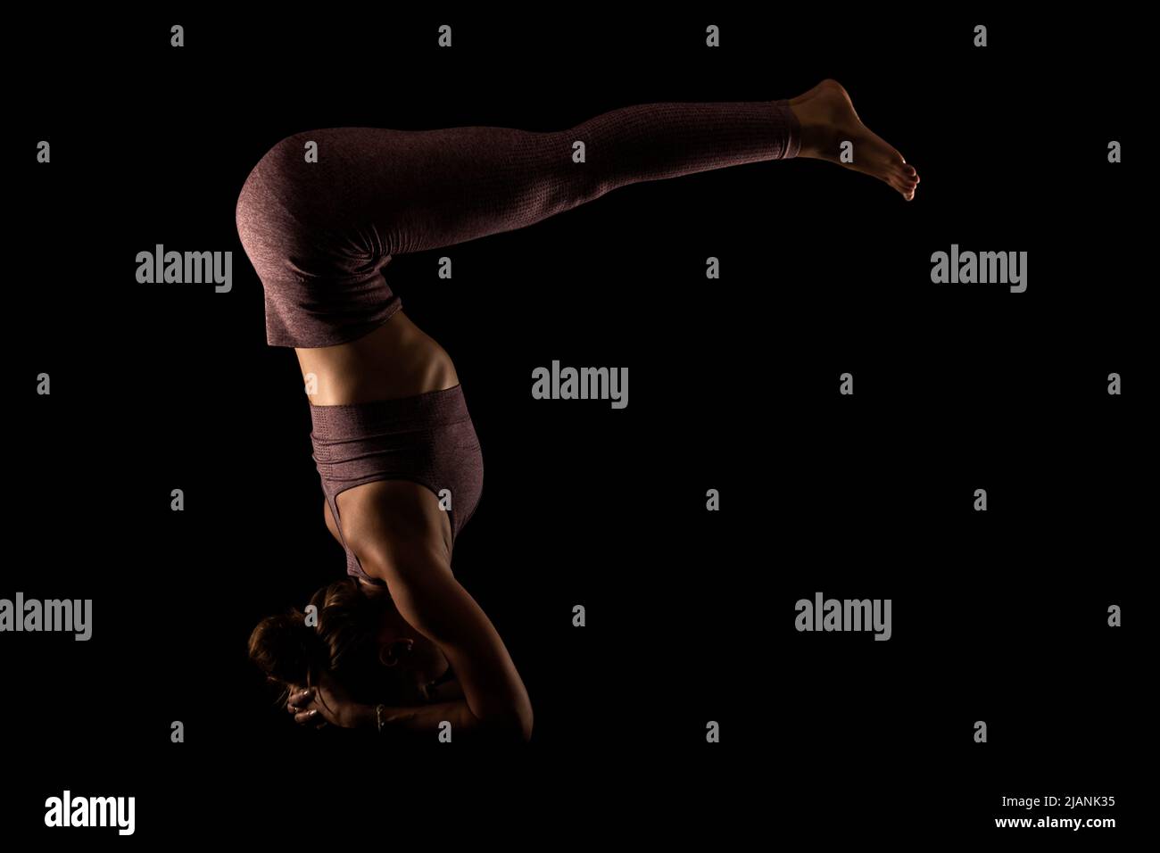 Fit woman practicing yoga poses. Side lit half silhouette girl doing exercise in studio against ...