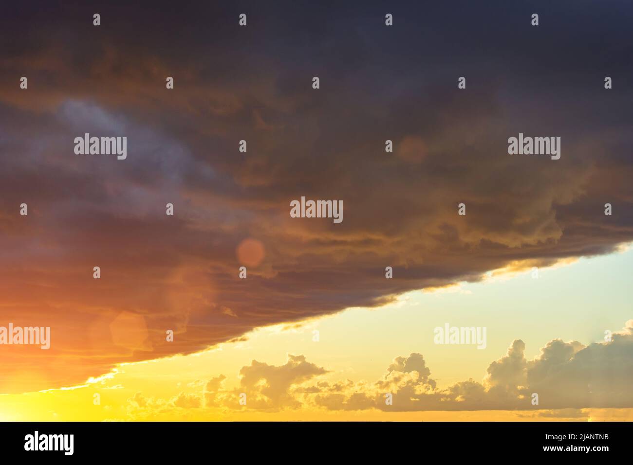 Dark sharp edge of a thundercloud front in front of a sunset sun ...