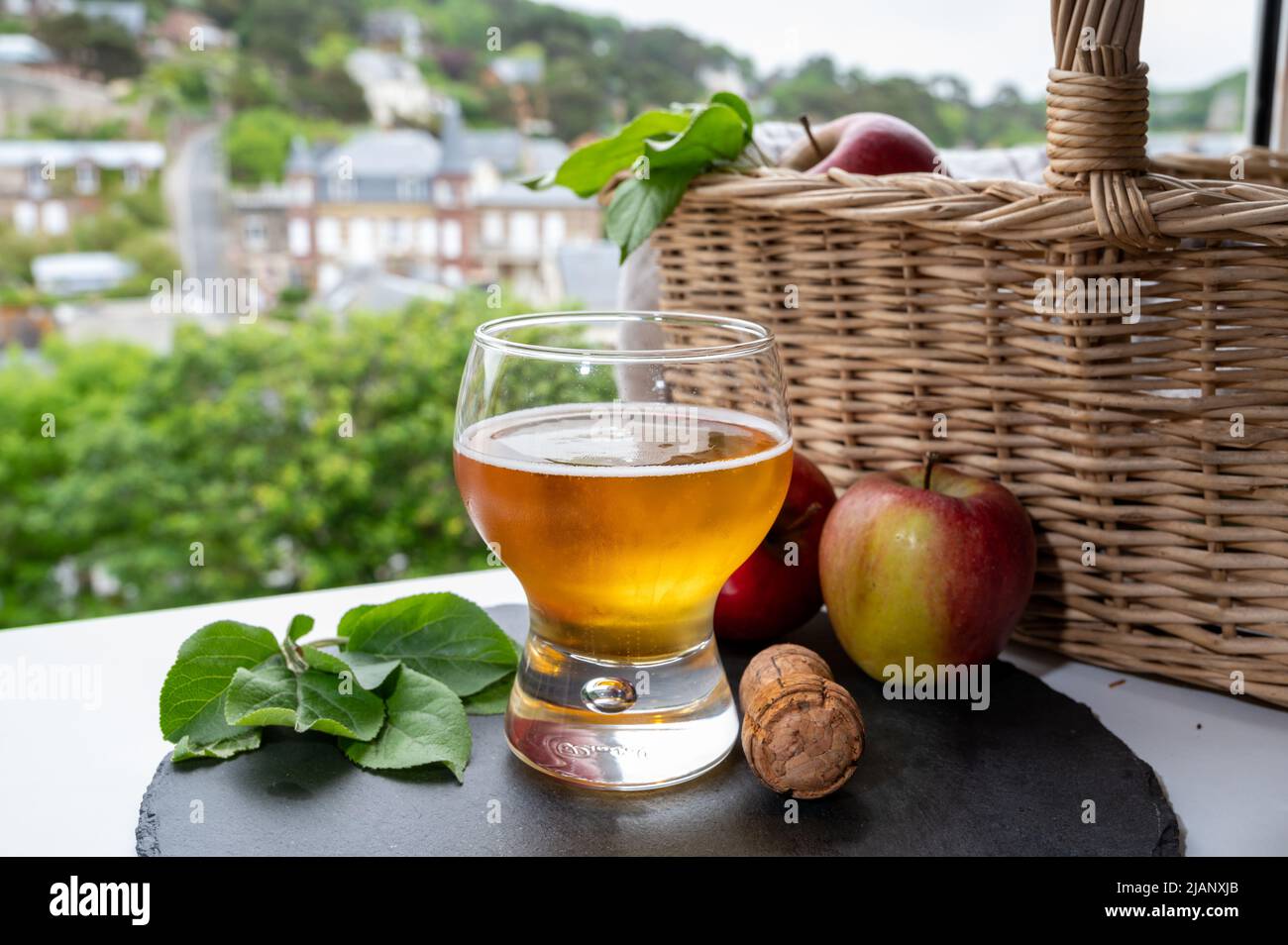 Glass of cold apple cider drink, ripe apples with leaves and houses of ...