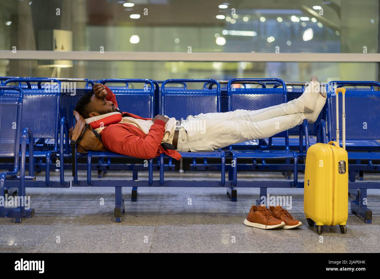 African man napping while waiting for flight. Black guy lying on bench ...