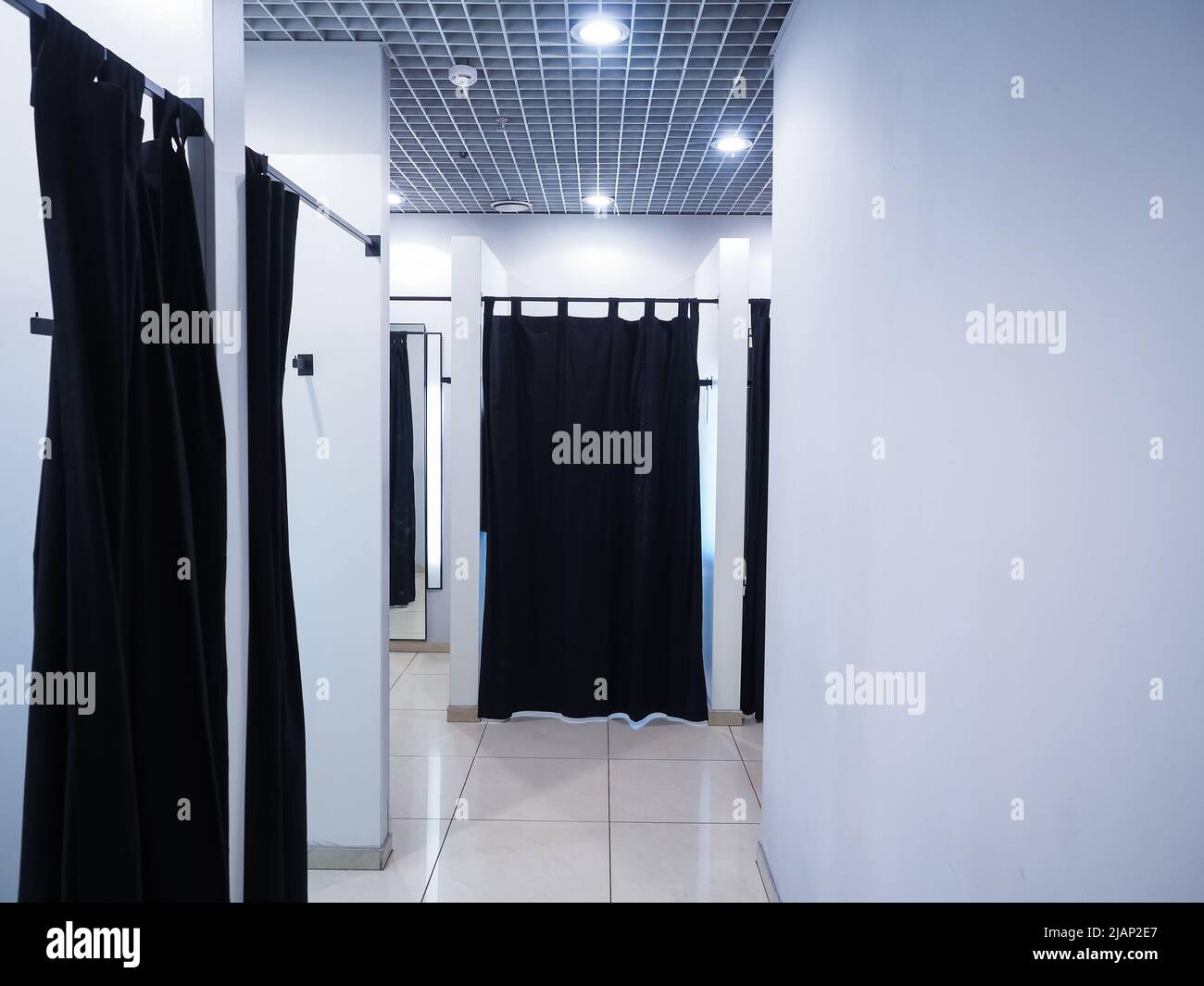 Light fitting room with white walls and black curtains on booths ...