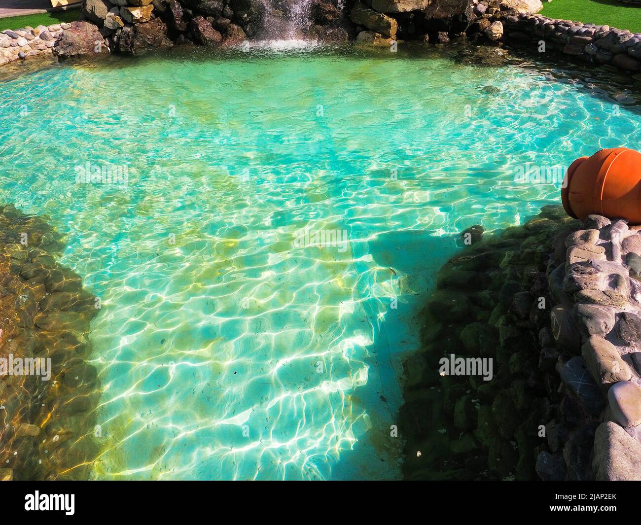 Decorative summer pond with turquoise water shining in the sun and ...