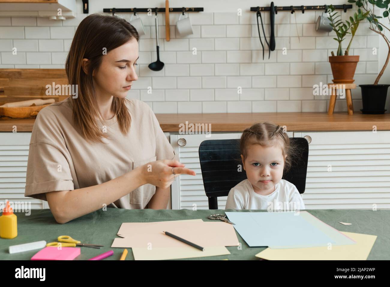 Cute angry little preschool girl doing creative homework with her mom ...