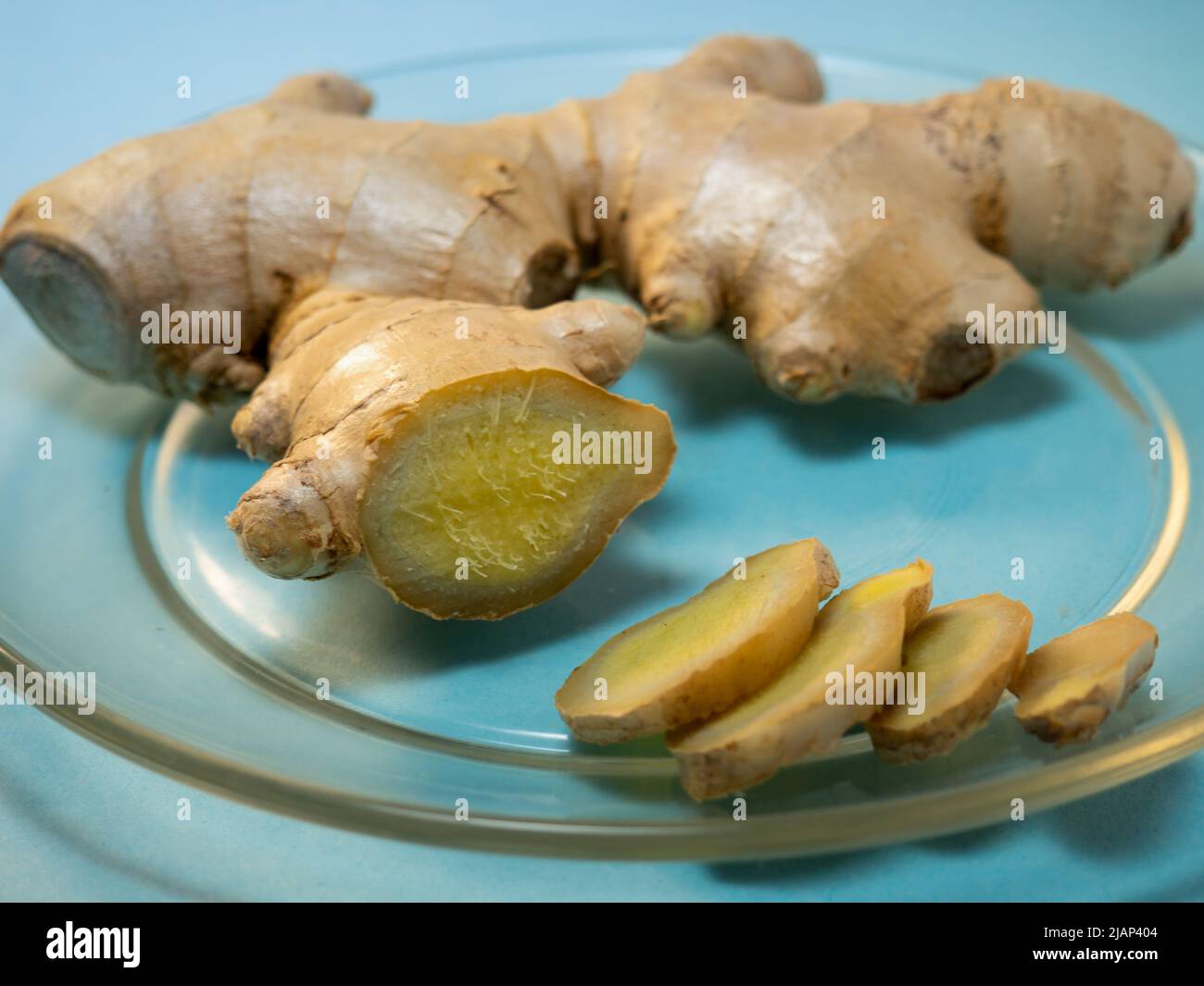 Cut ginger root on a transparent plate. Blue background. Pieces of ...