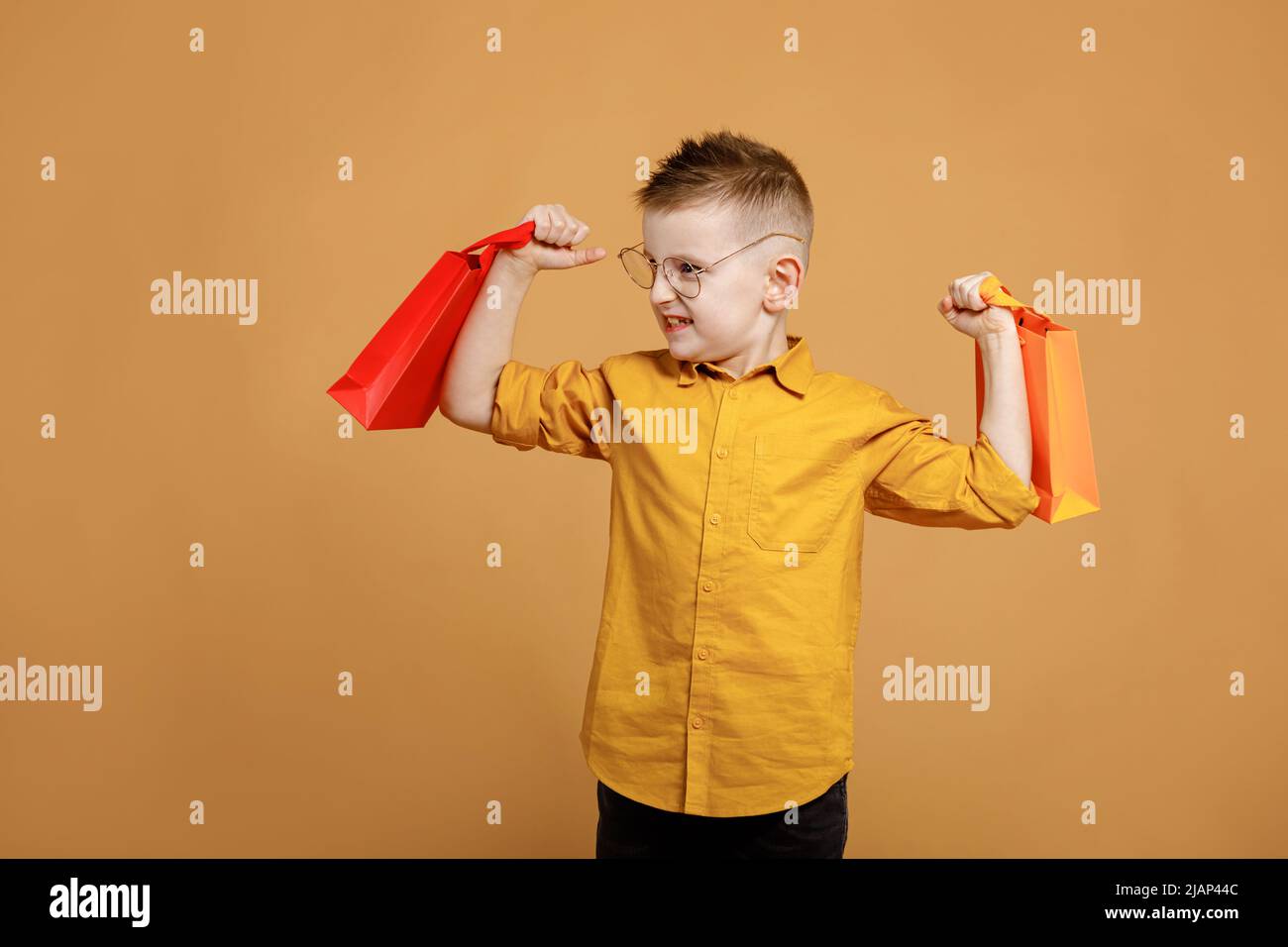 Image of smiling boy holding bags with presents or shoppings on yellow ...