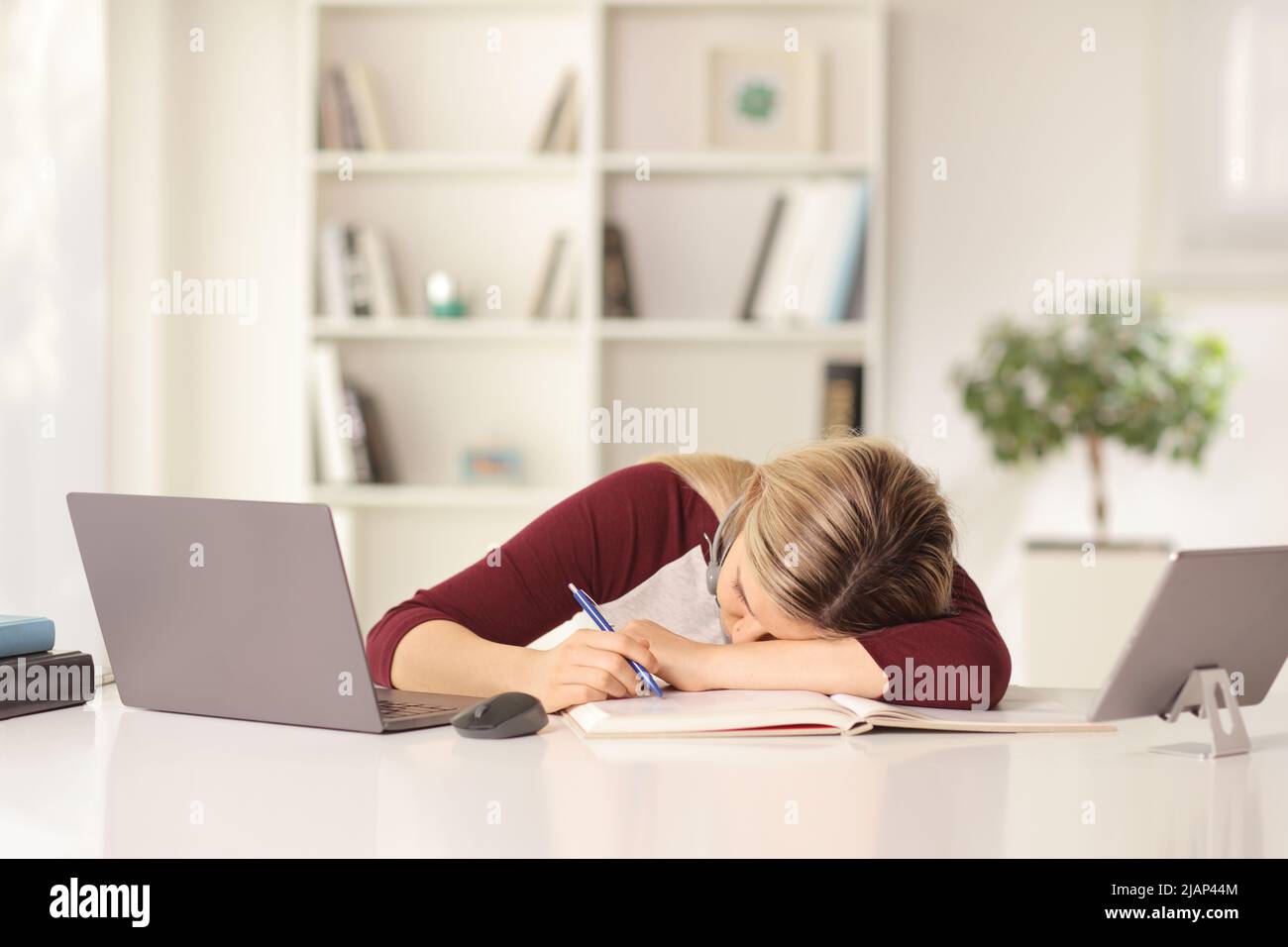 Tired female student sleeping on a desk at home with a laptop computer ...