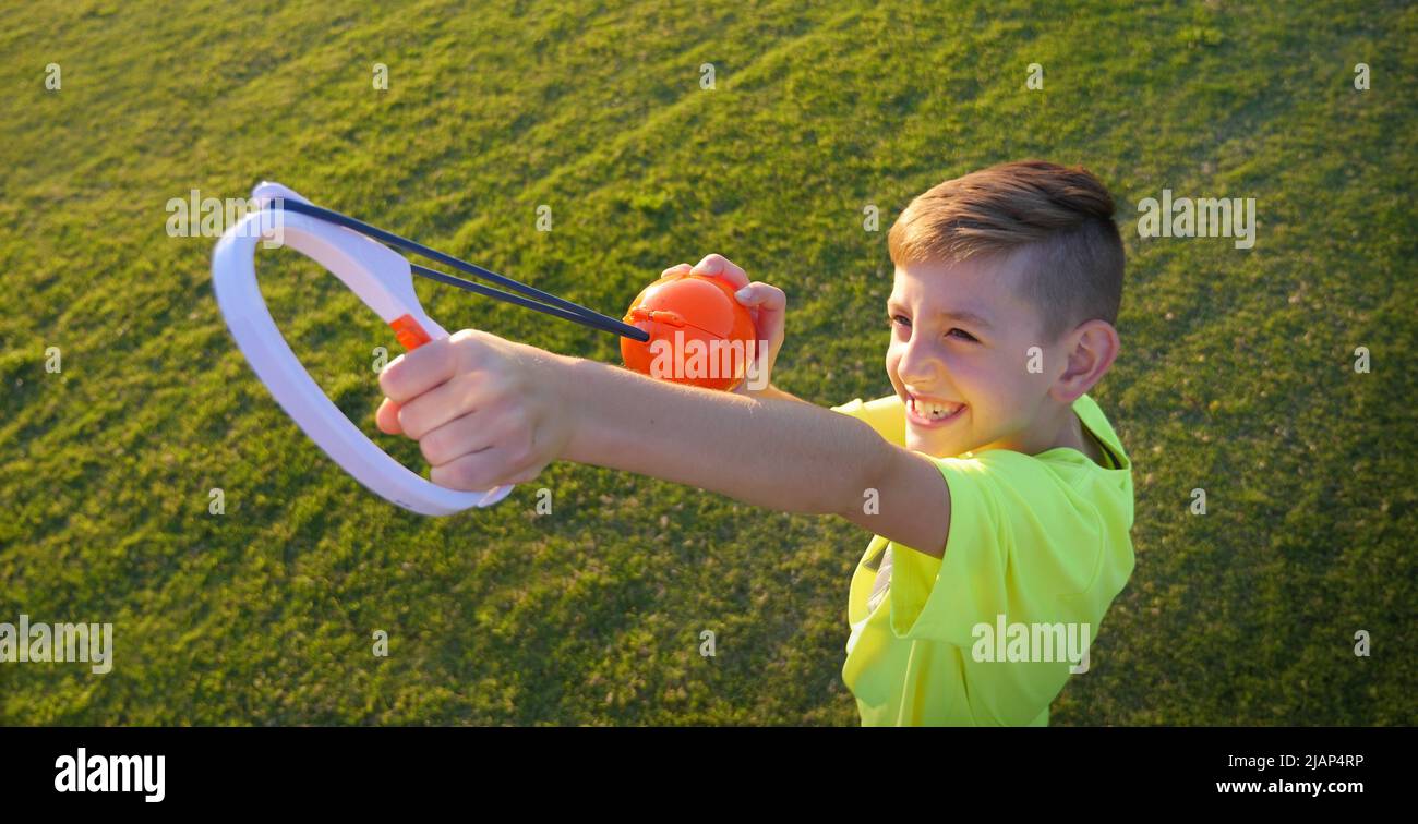 Boy playing outside shooting modern slingshot from grassy field Stock ...