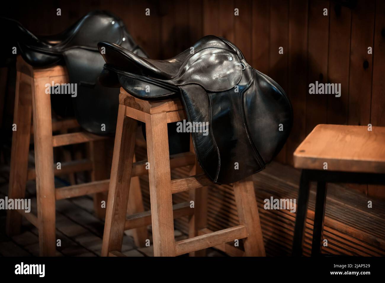 Black leather saddle on wooden bar stool in a cafe interior. Decorative ...