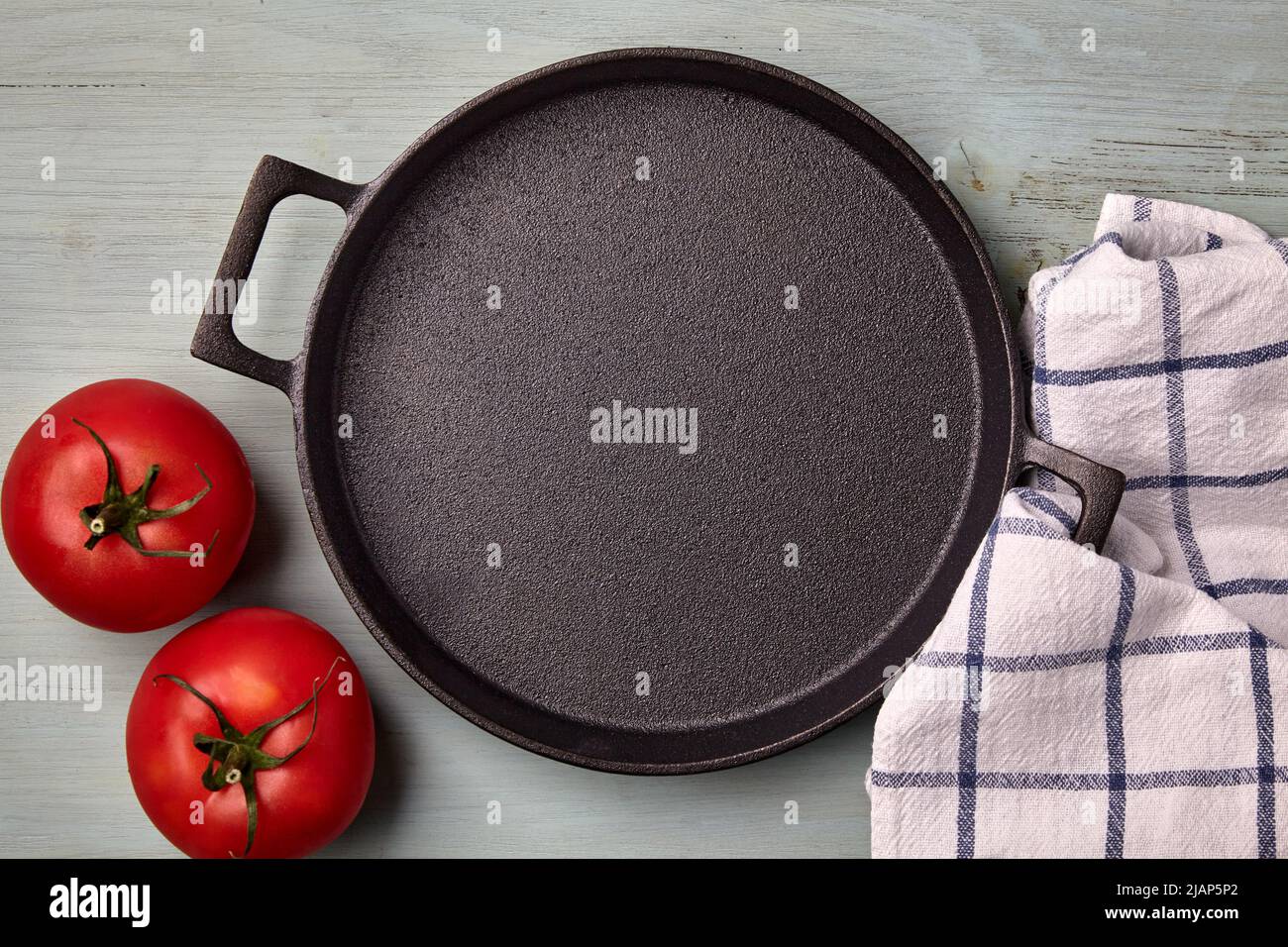 Empty round cast iron pan, tea towel and tomatoes on a light blue ...