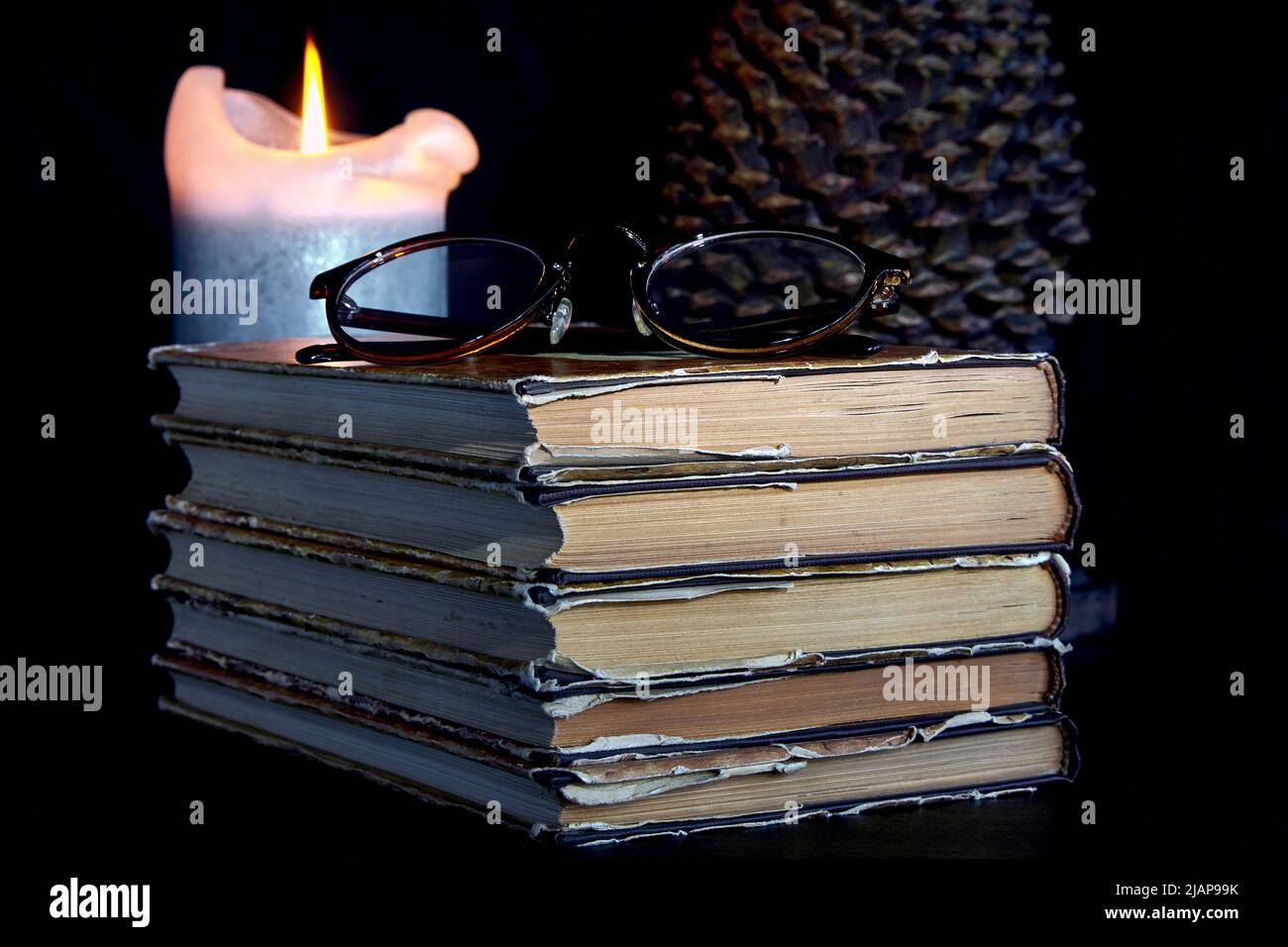 A stack of old books, a burning candle, glasses and book holder on a ...