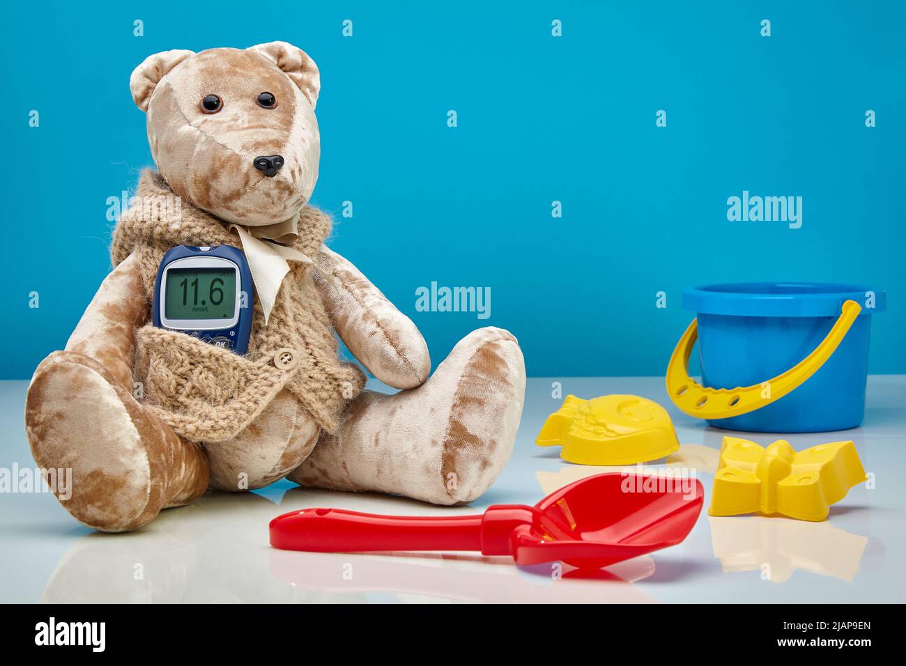 Teddy bear with a glucometer and scattered children's toys on a blue ...