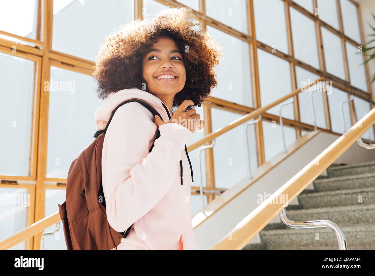 Smiling girl looking back while standing on stairs in school. Student ...