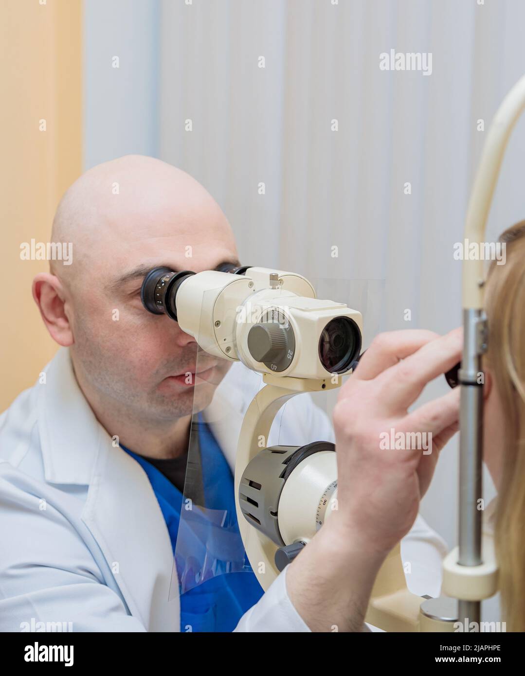 A male ophthalmologist checks the eyesight of a young girl using a ...