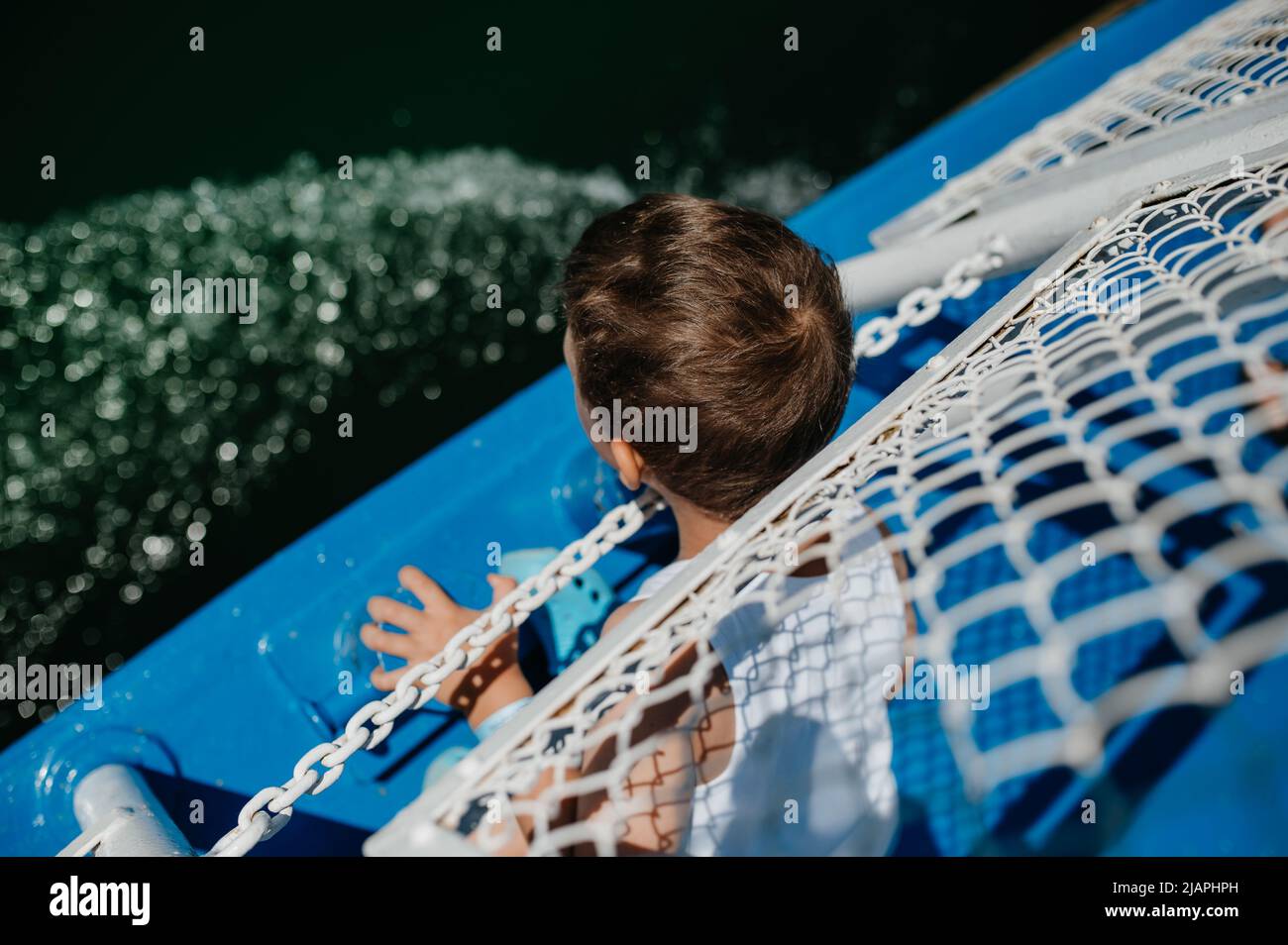 Little curious boy looking at water from motor boat Stock Photo - Alamy