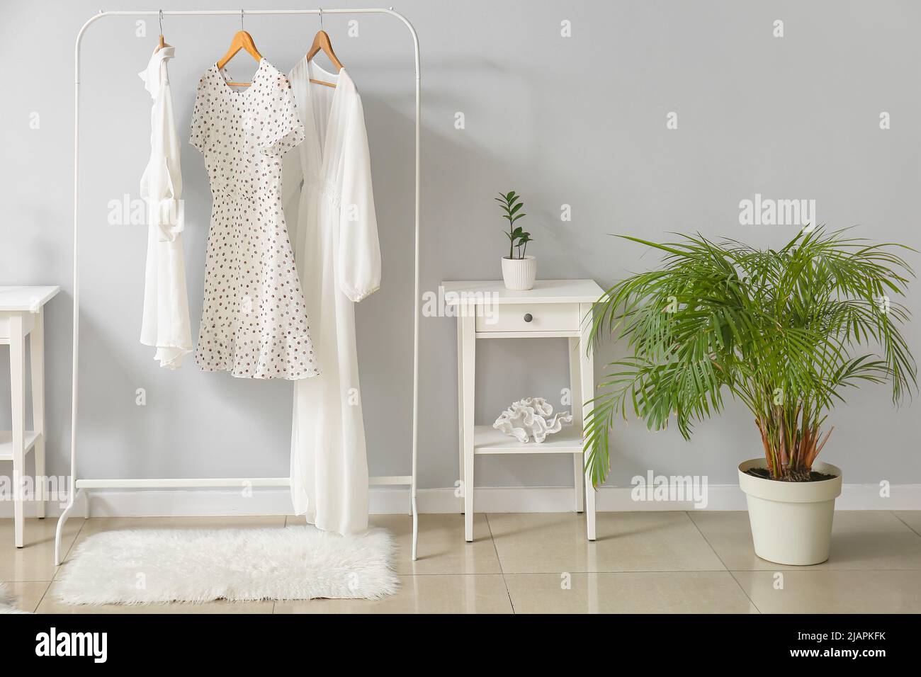 Rack with stylish female clothes, table and houseplant near light wall ...