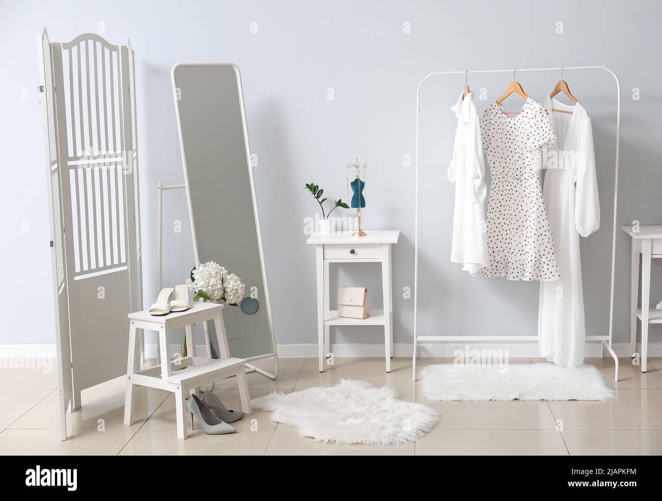 Rack with stylish female clothes, table, step ladder and mirror near ...