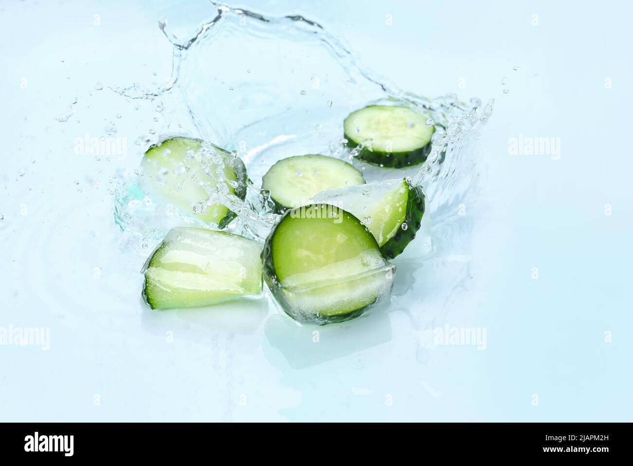 Fresh cucumber slices frozen in ice with splash of water on white ...