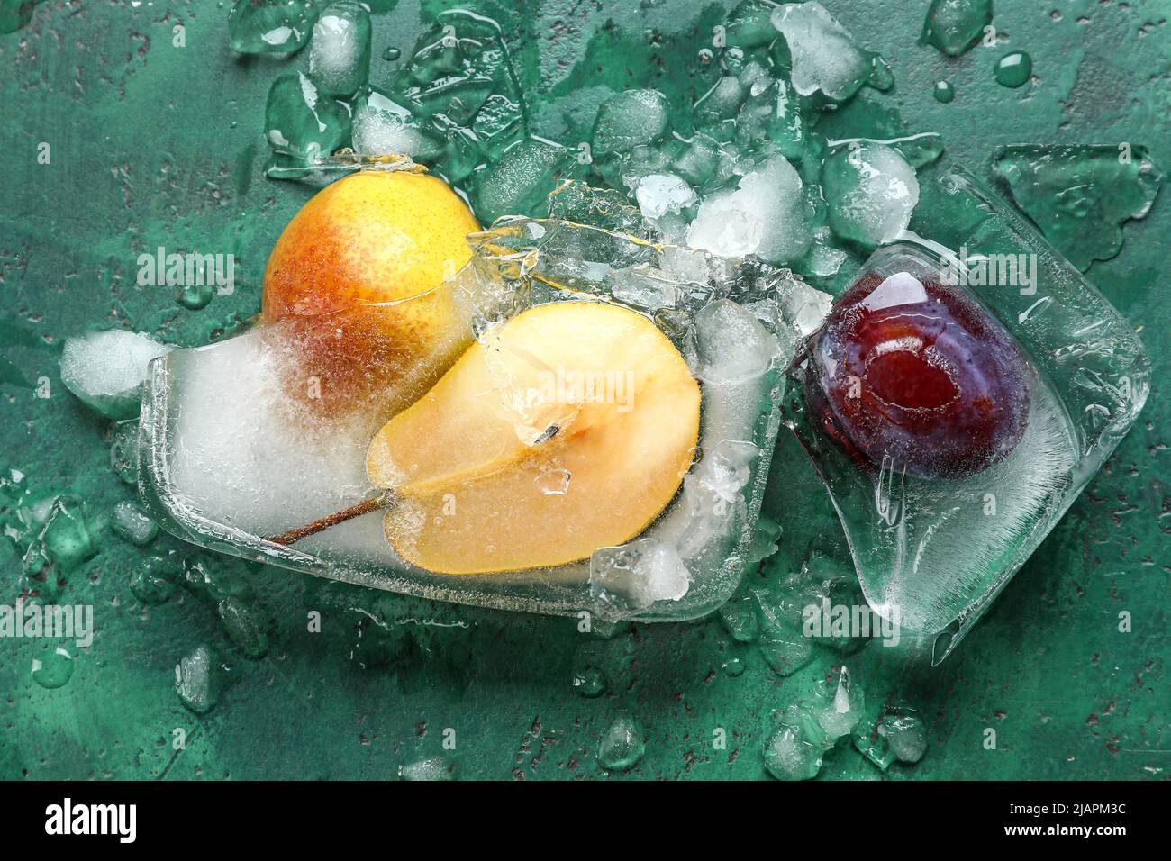 Fresh fruits frozen in ice on green background Stock Photo - Alamy