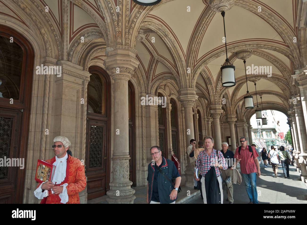 Tourists following a tour guide under the arcades of the Vienna State ...