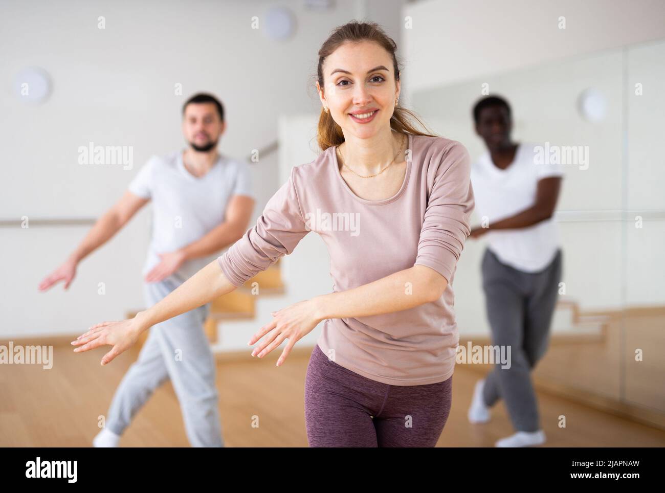 Young woman practicing vigorous dance movements with group Stock Photo ...