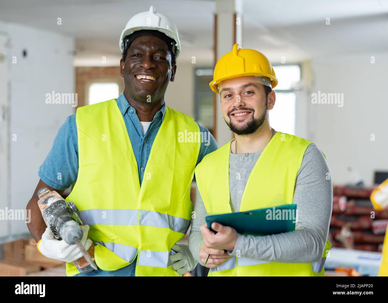 Portrait of two positive builders holding a hammer drill and working ...