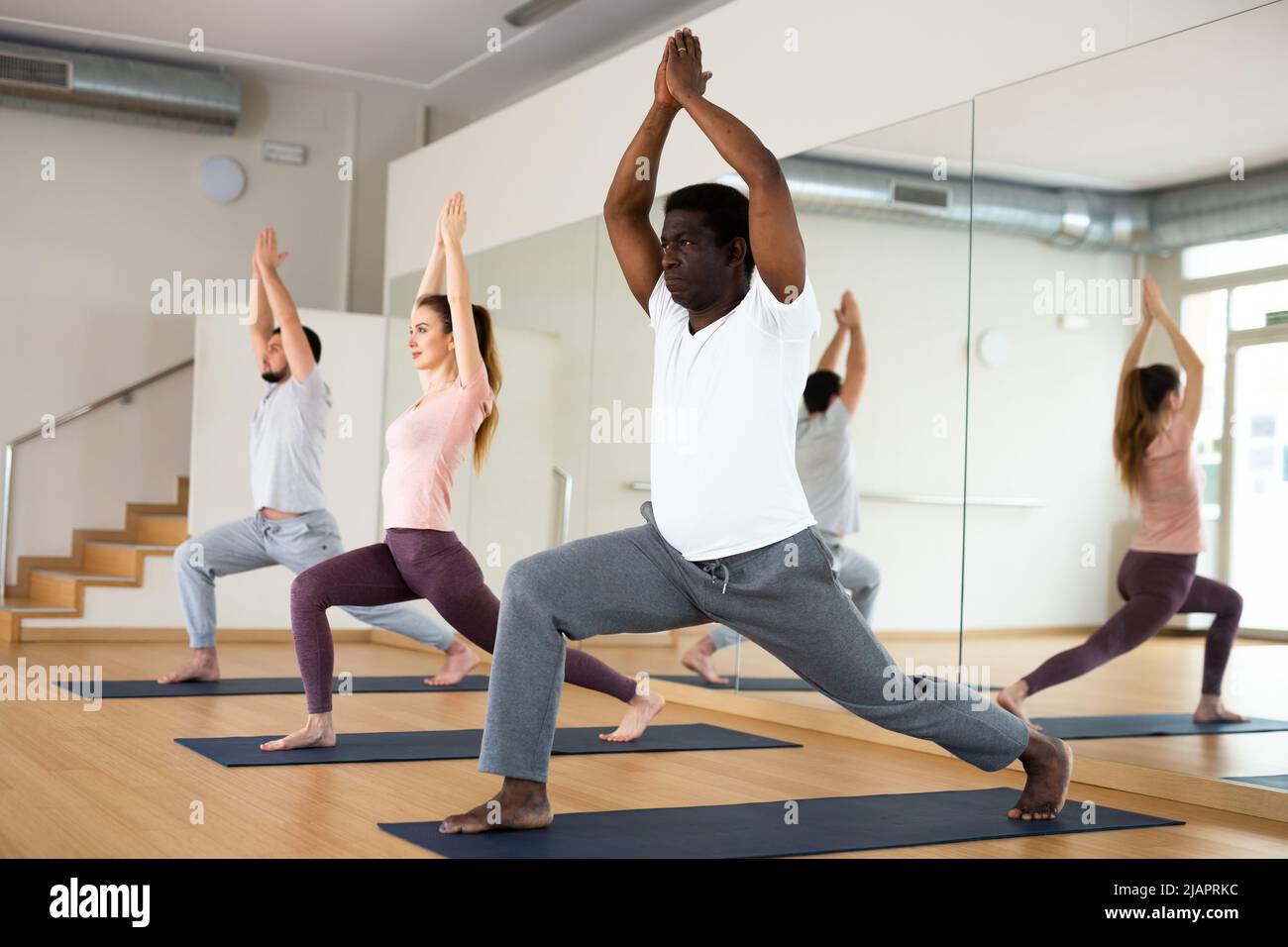 Man exercising warrior one yoga pose with people in gym Stock Photo - Alamy