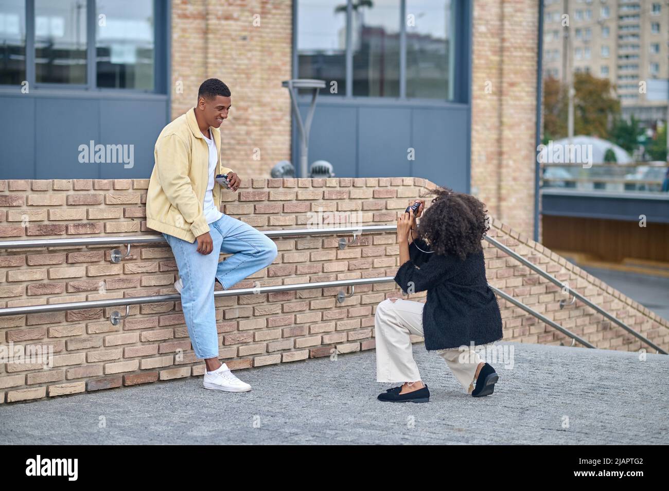 Girl crouched photographing posing guy on street Stock Photo - Alamy