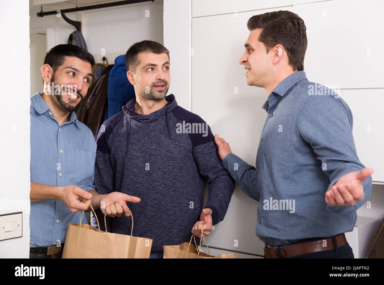 Two smiling men visiting friend at home Stock Photo - Alamy