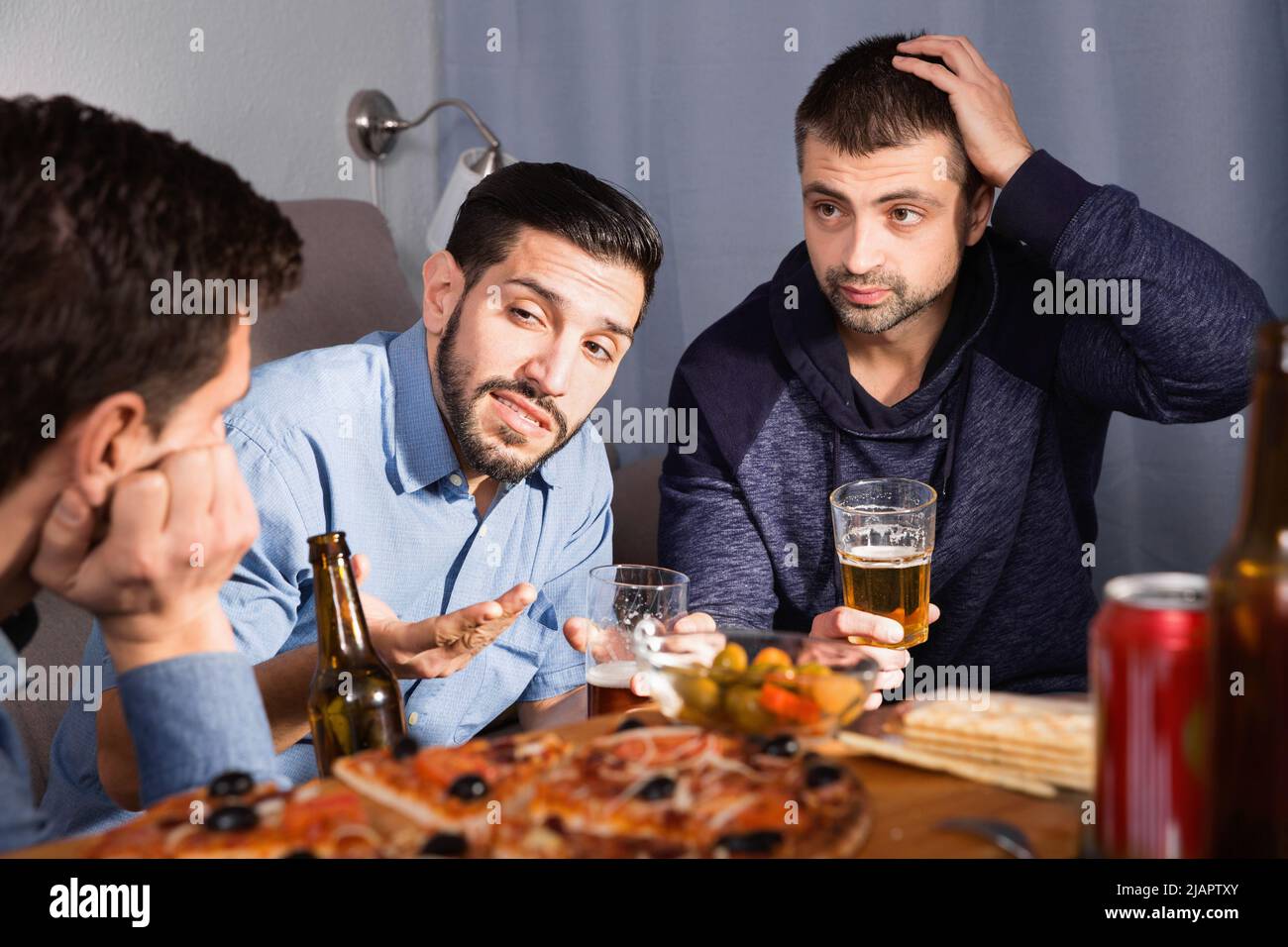 Troubled male friends talking, drinking beer with pizza Stock Photo - Alamy