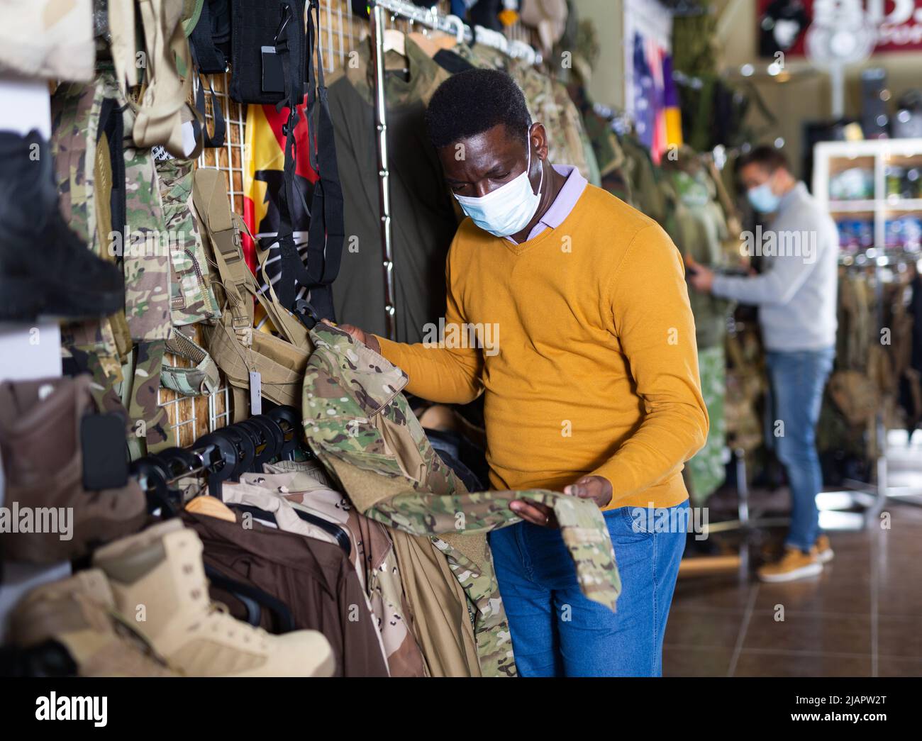 Male shopper in protective mask chooses camouflage uniform at army ...