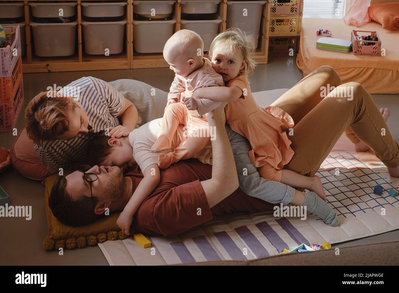 Happy parents with tree small kids playing at home. Dad mom cuddling ...