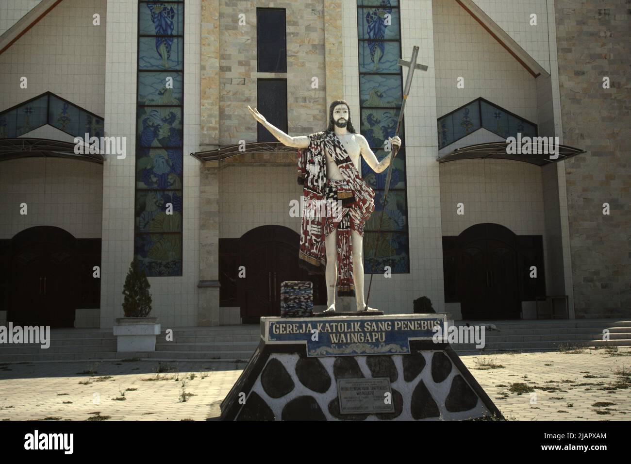 Statue of Jesus holding a cross and wearing Sumbanese traditional woven ...