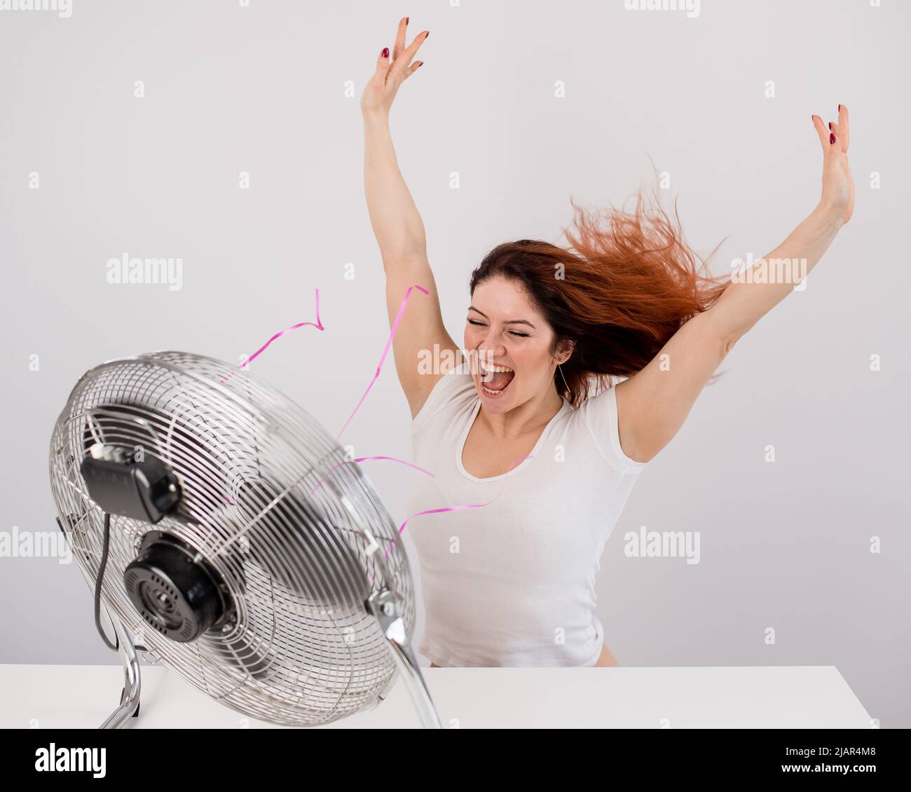 Joyful caucasian woman enjoying the wind blowing from an electric fan ...
