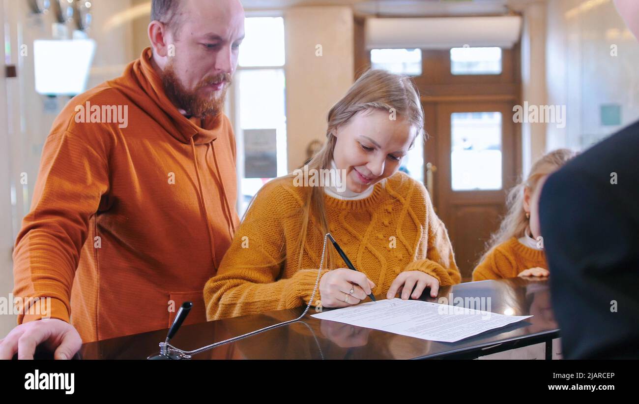 A family checking in the hotel - a woman singing the papers for room ...